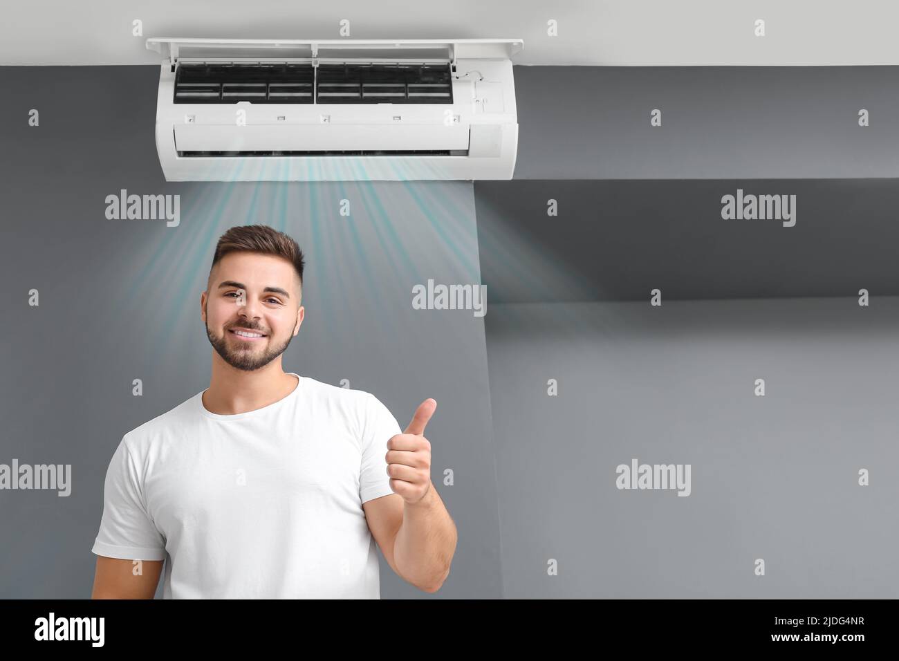 Happy young man showing thumb-up in room with operating air conditioner ...