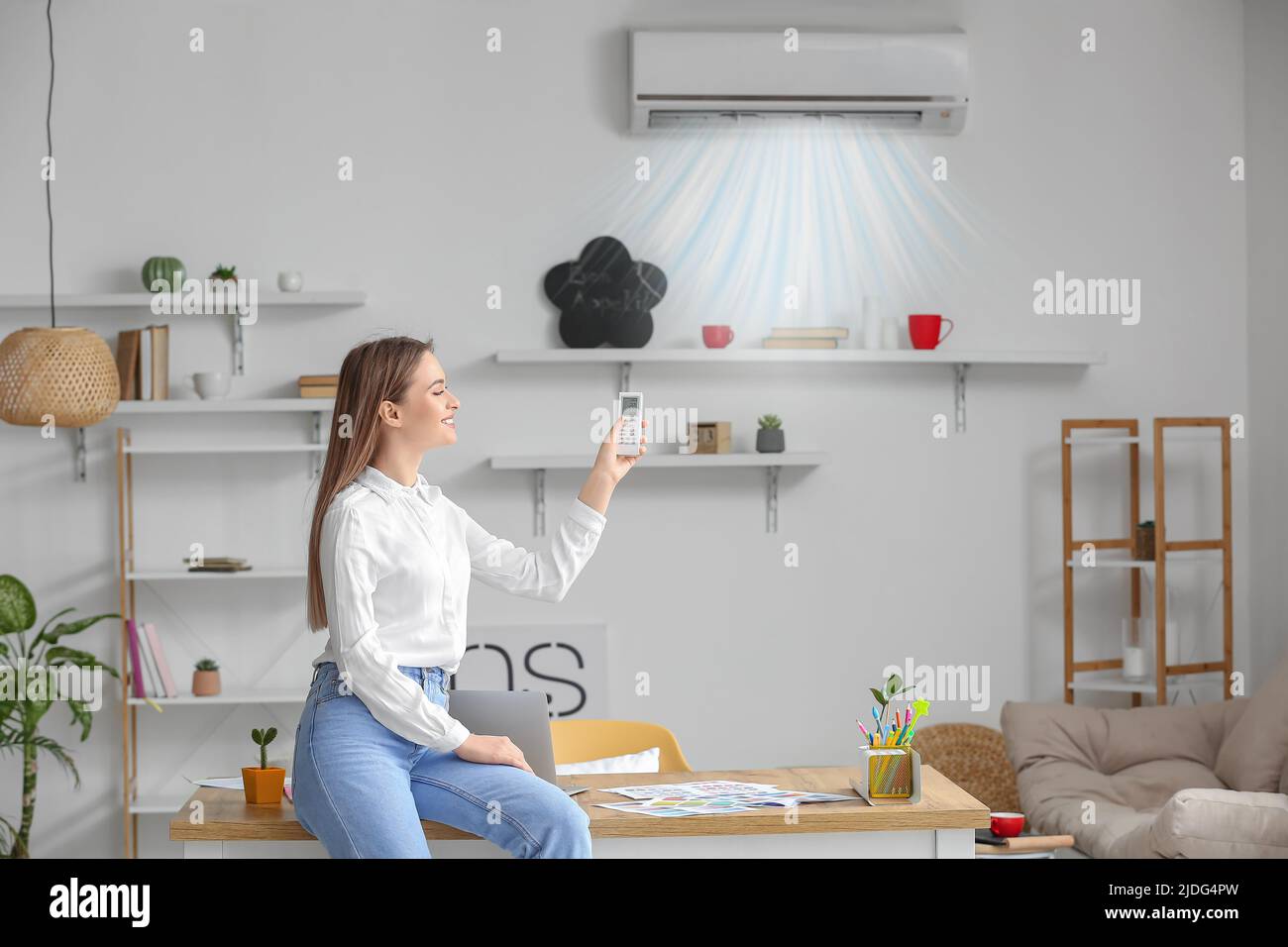 Beautiful young woman switching on air conditioner in room Stock Photo ...