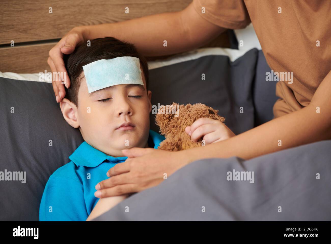 Sick child hugging teddy bear when sleeping in bed with cooling patch ...