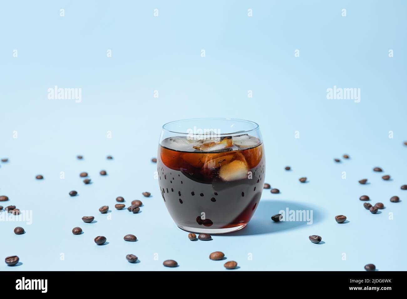 Glass with cold brew and scattered coffee beans on blue background ...