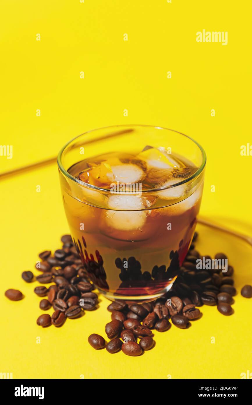 Glass with cold brew and coffee beans on yellow background, closeup ...