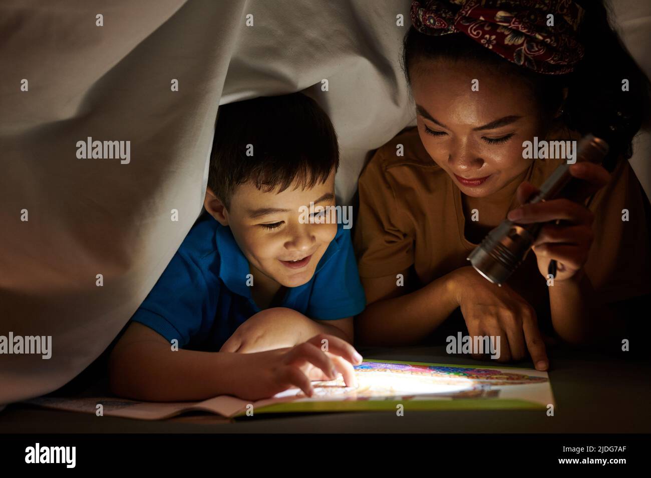 Mother shining flashlight on book page when son reading scary story ...