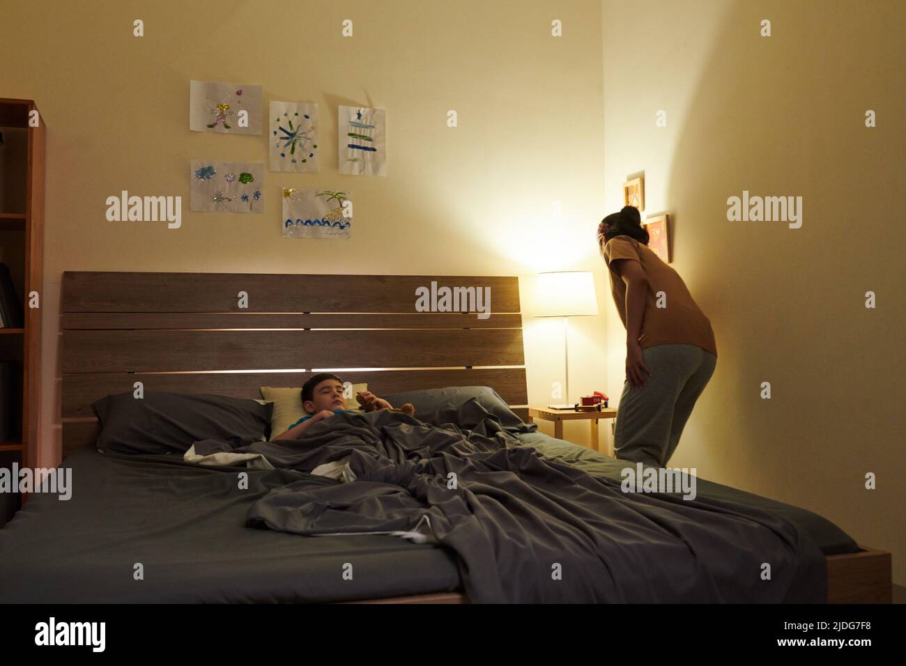 Caring mother turning off lamp on bedside table in room on her sleeping ...