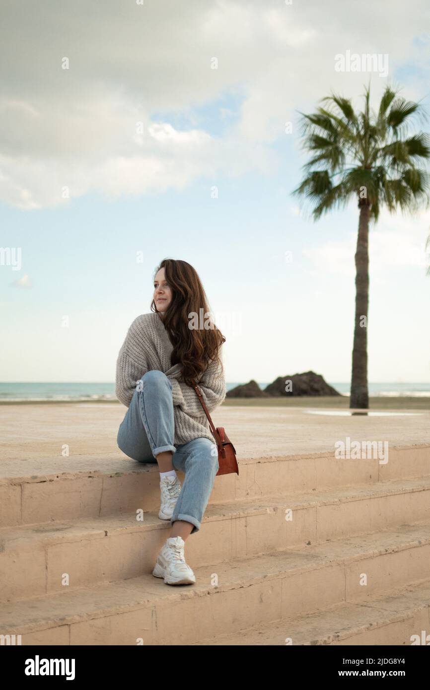 Woman is sitting on stairs with palm tree and sea background in Larnaca ...