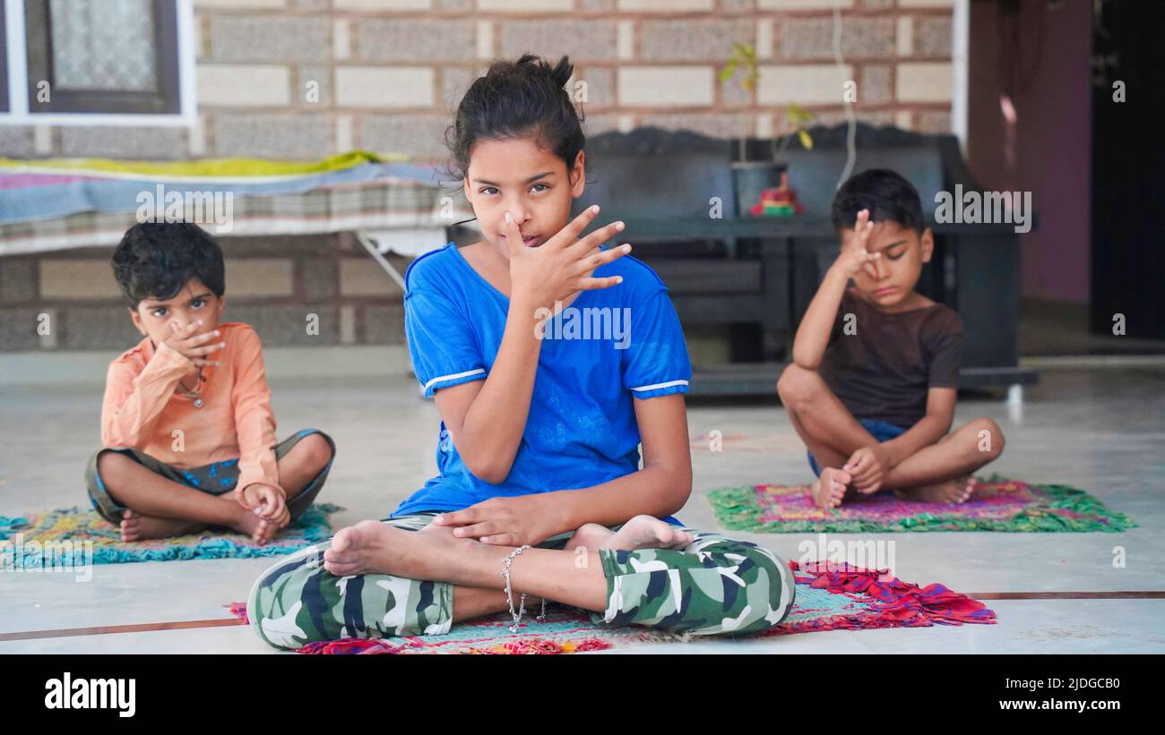 Three Indian little kids doing meditate yoga asana on roll mat at home ...
