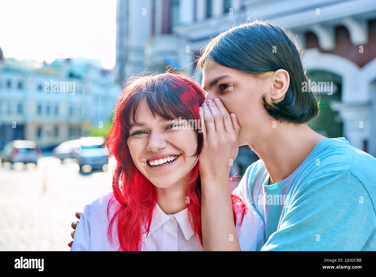 Couple of teenage students friends, guy whispers secret in ear of ...