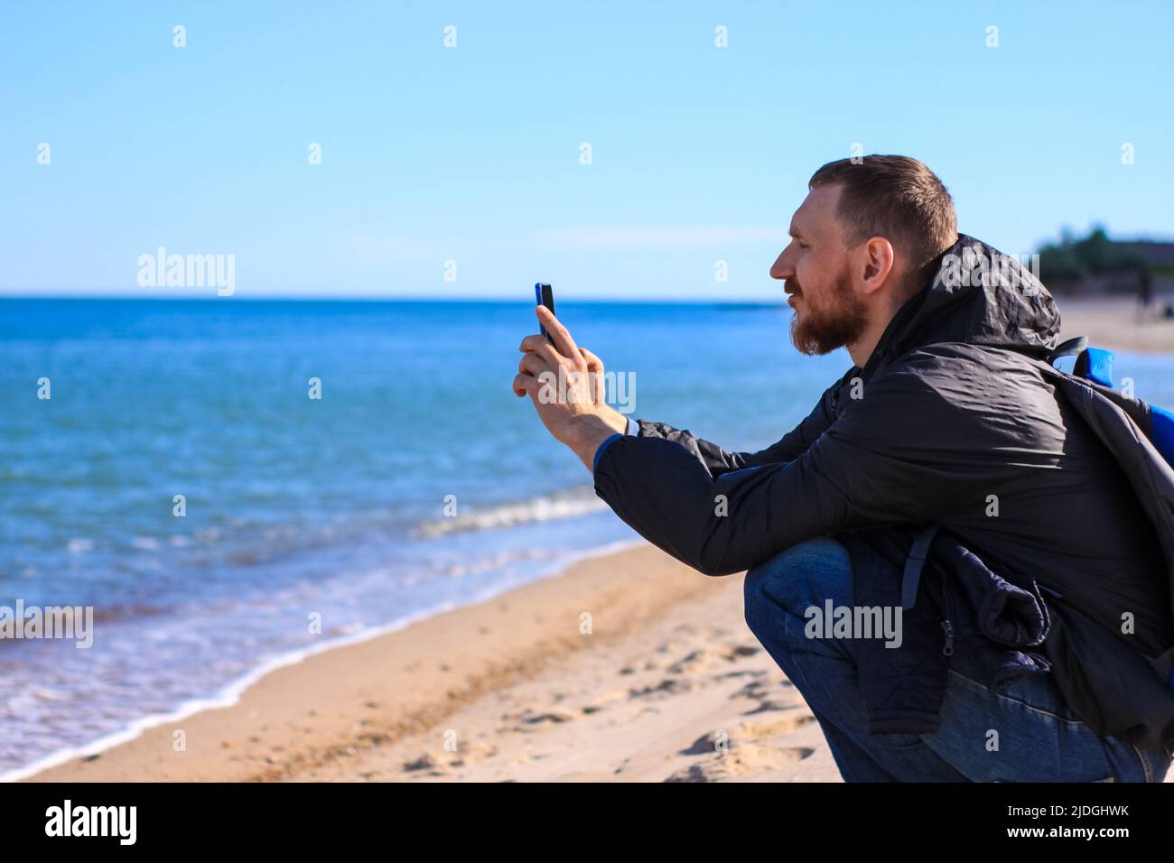 Bearded man in black raincoat on a blue sea landscape background with ...