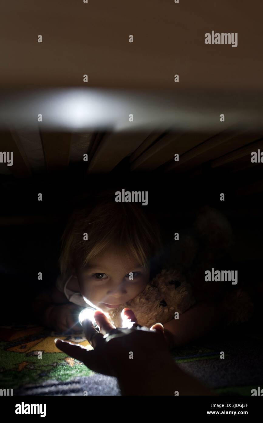 Little child, hiding under the bed, hugging teddy bear and holding ...