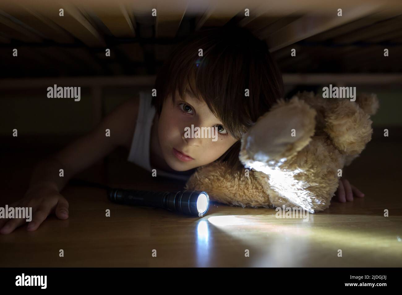 Little child, hiding under the bed, hugging teddy bear and holding ...