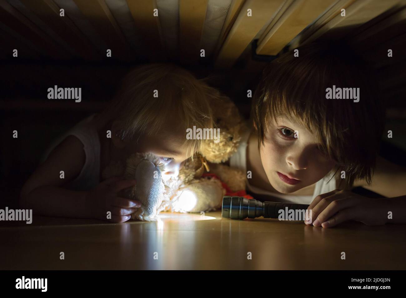 Little child, hiding under the bed, hugging teddy bear and holding ...