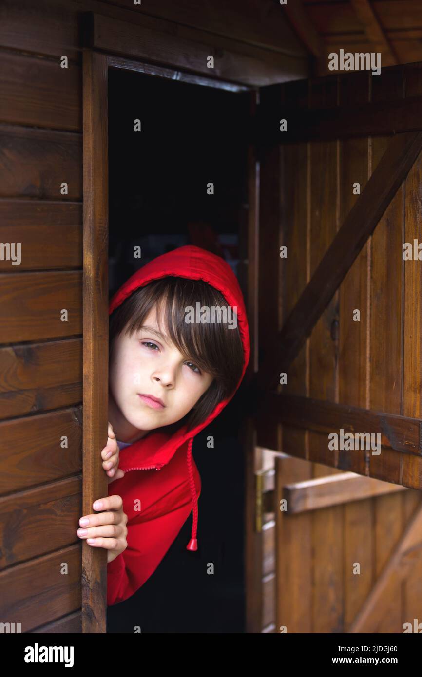 Preteen boy in red sweatshirt, hiding behind a wooden door, looking ...