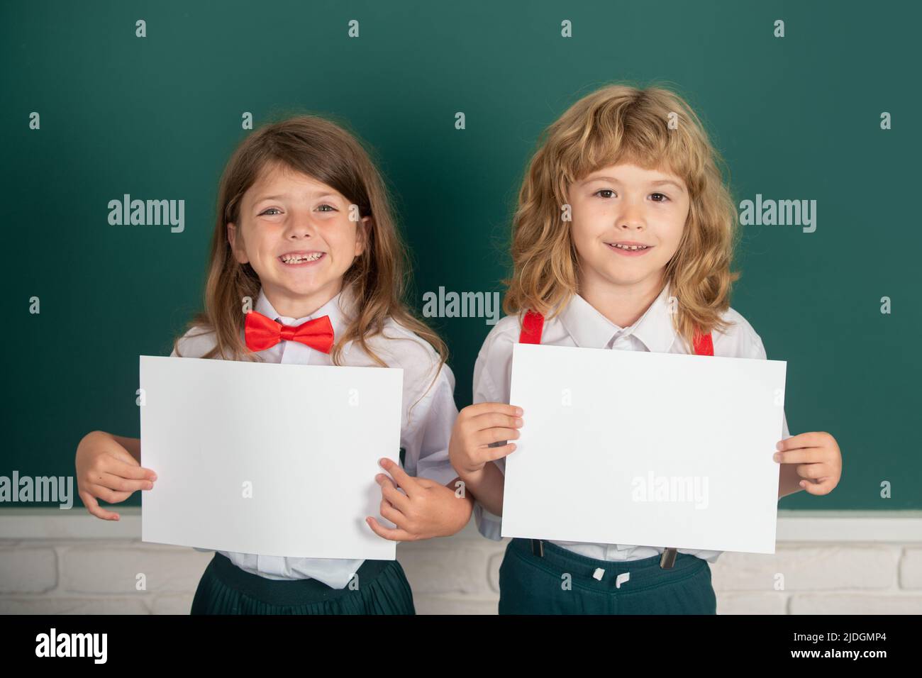 Two schoolkids holding white paper blank, poster with copy space ...