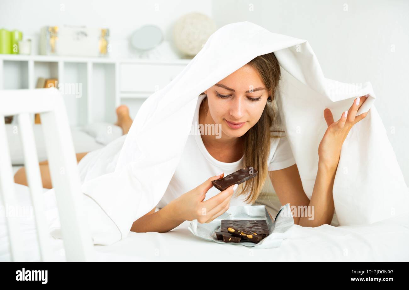 Happy girl hiding under sheet with sweets indoors Stock Photo - Alamy