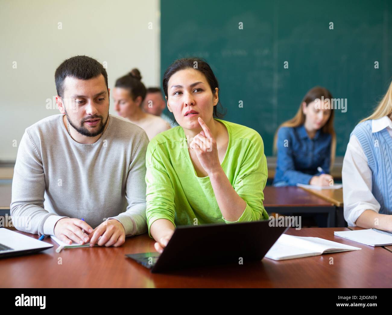 Man and woman helping each other to solve problem on laptop while ...