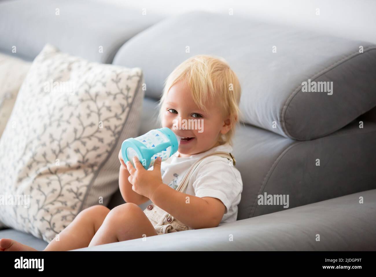 Adorable baby boy drinking milk from a bottle in a white sunny living ...