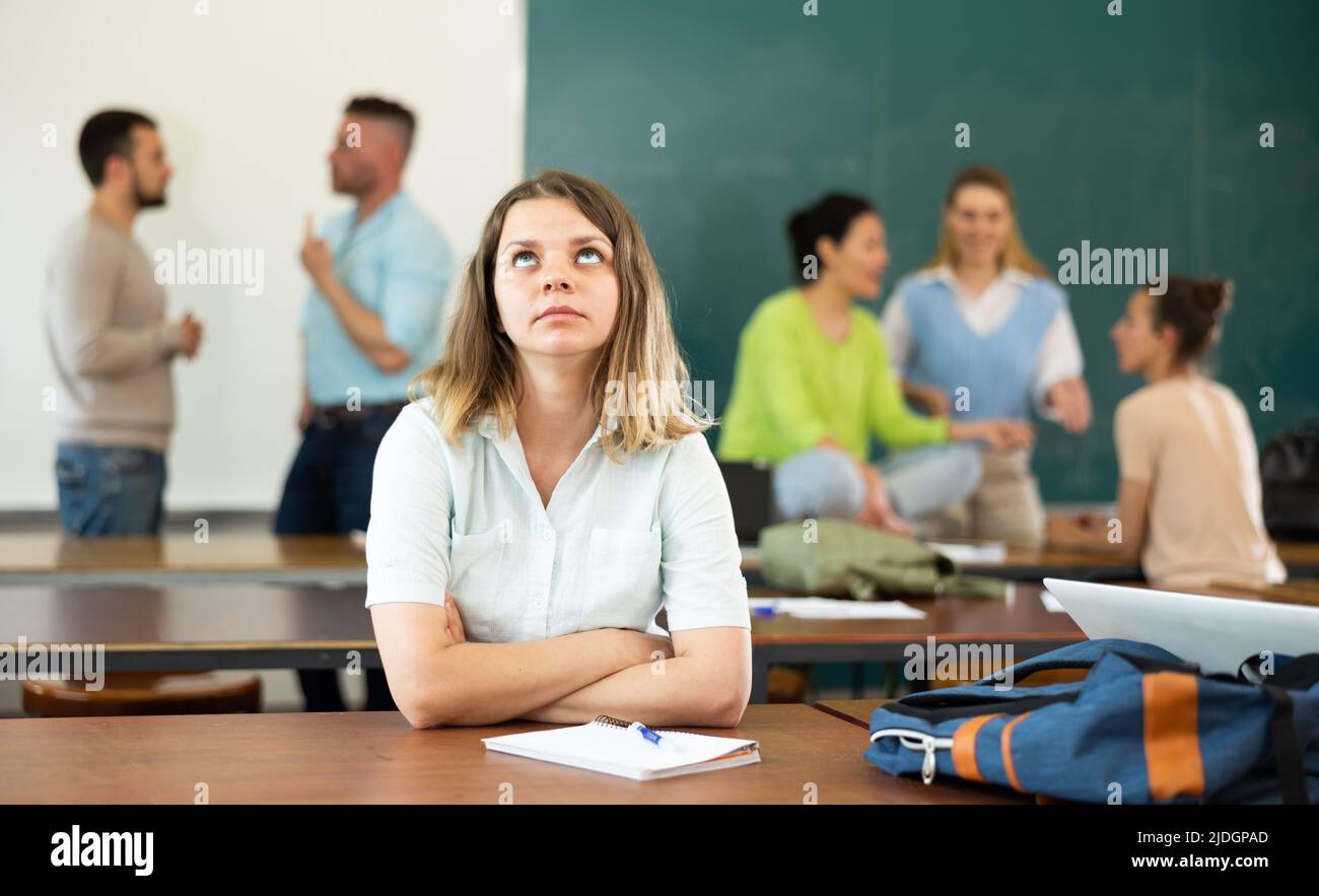 Upset girl sitting at table in auditorium during break on background with students Stock Photo ...