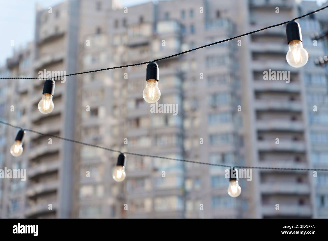 Group of glowing light bulbs on wires with a residential building ...