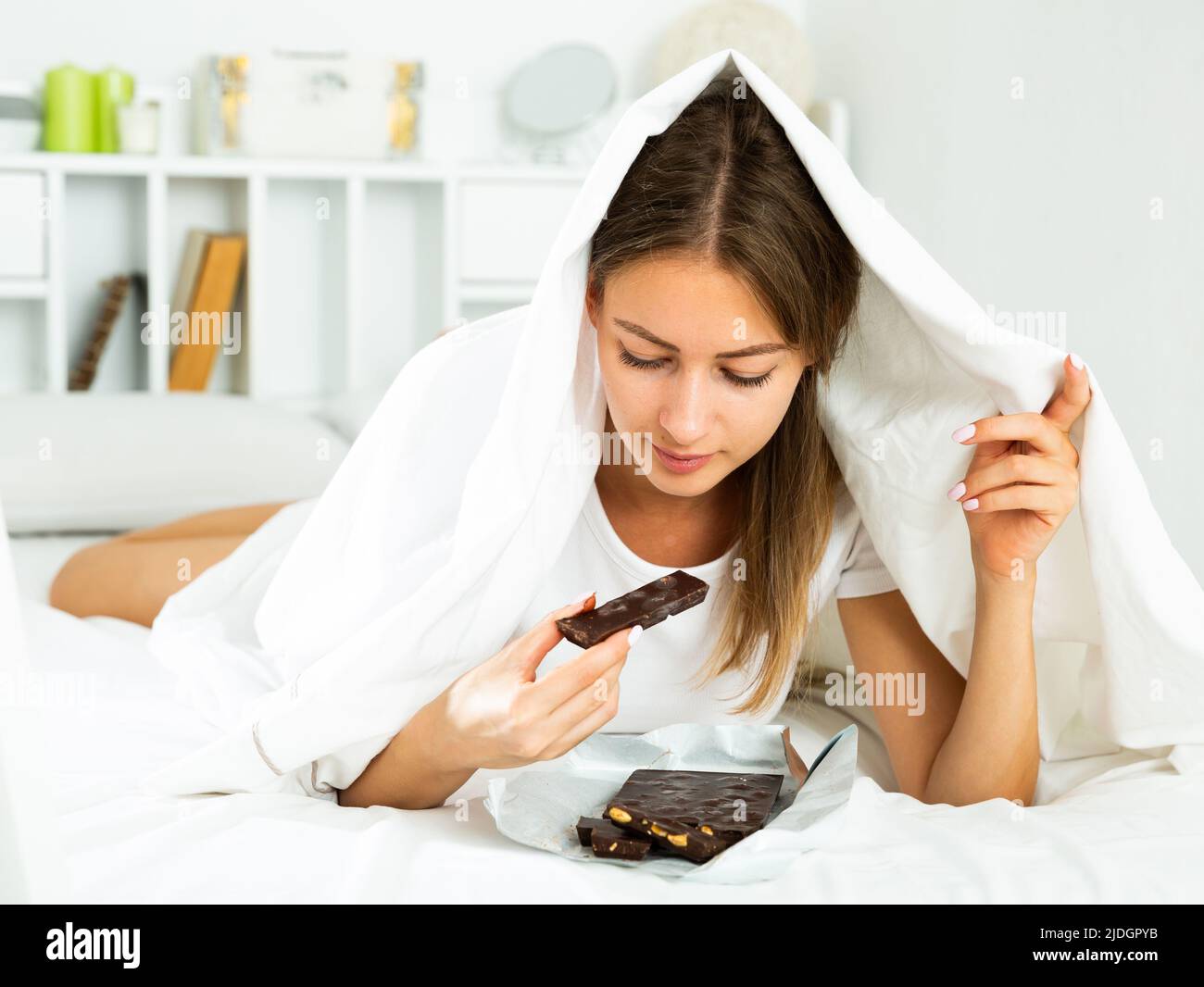 Woman secretly eating chocolate under sheets in bed Stock Photo - Alamy