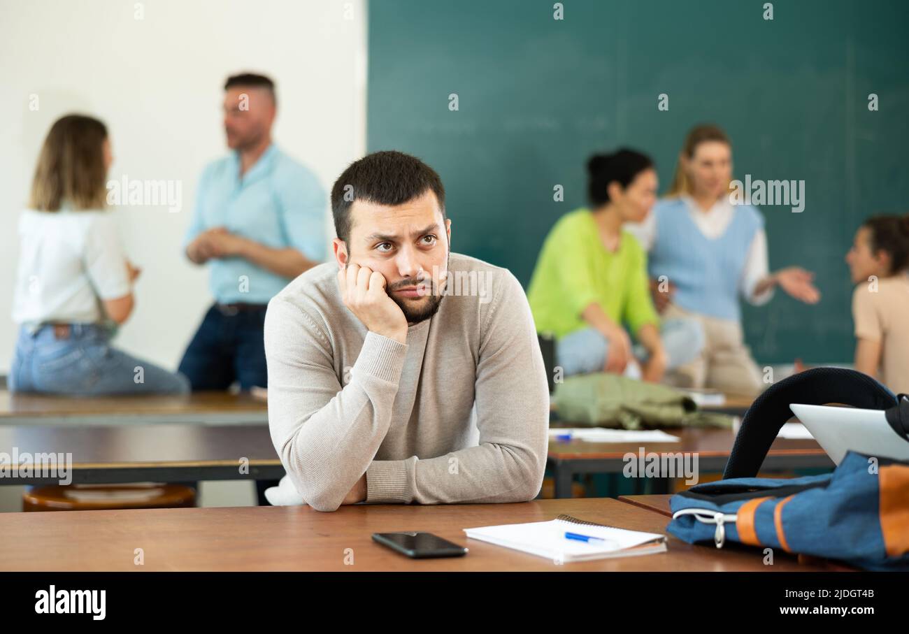 Frustrated man student sitting separately in classroom in break between ...
