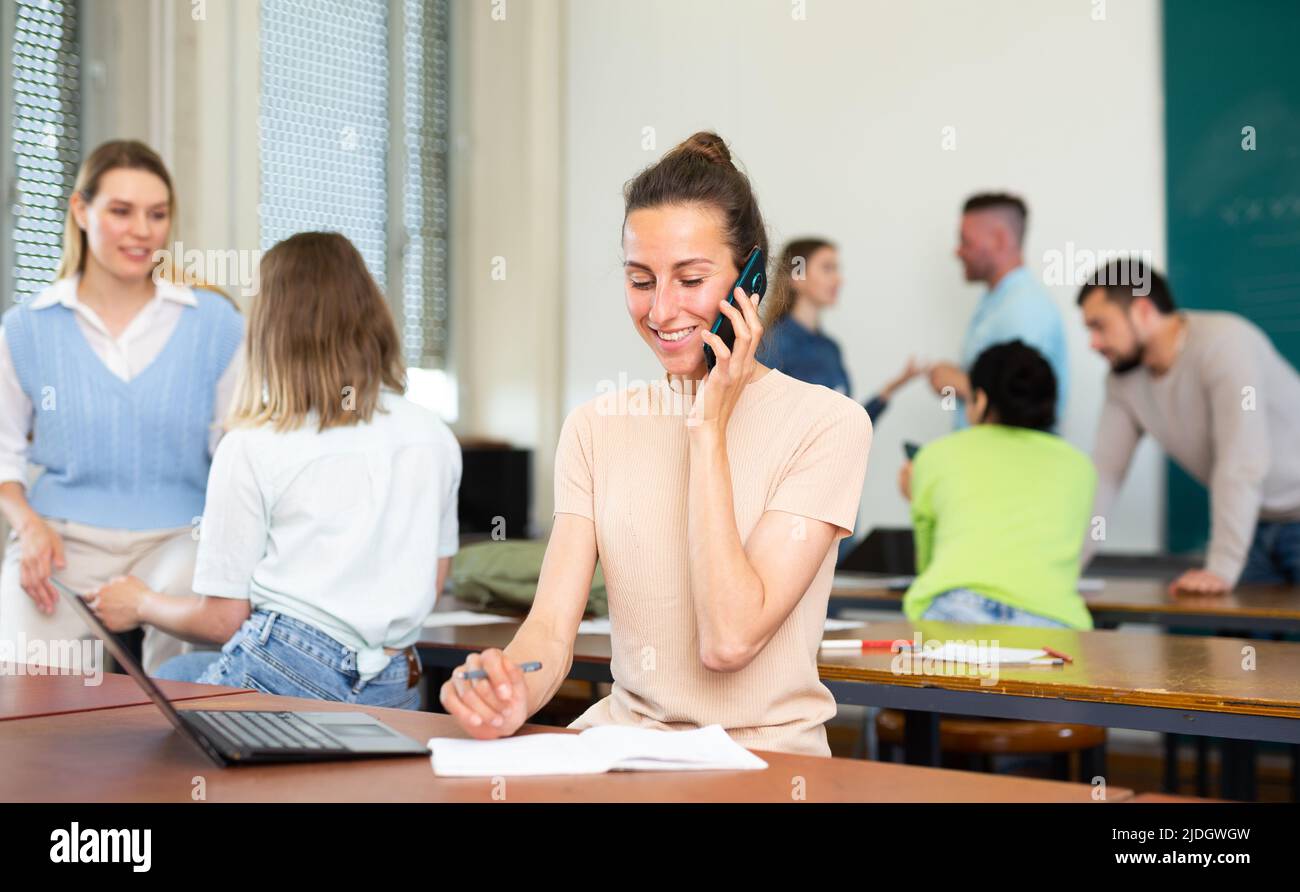 Positive young female student talking on mobile phone during break in ...