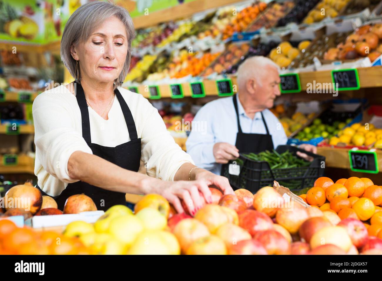 Woman merchandiser in apron putting goods on shelf in supermarket Stock ...