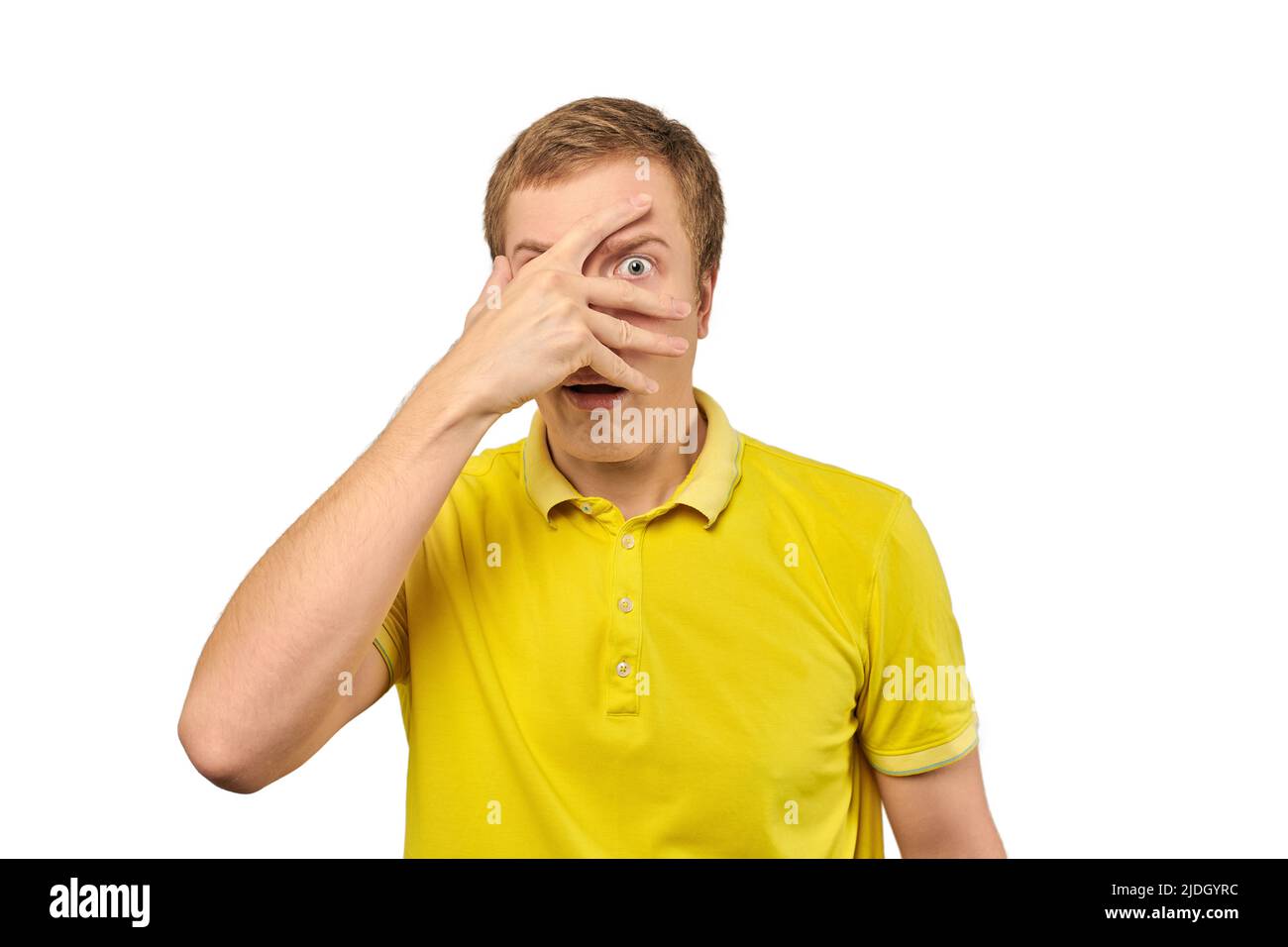 Afraid young guy in yellow T-shirt looking through fingers, white ...