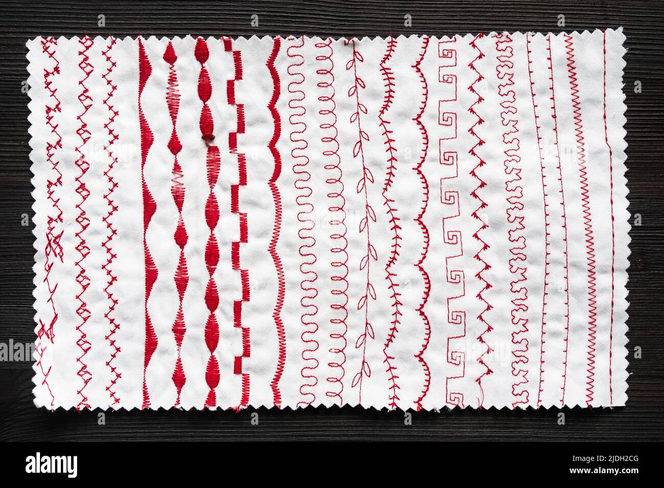 fabric with samples of stitches of sewing machine on dark wooden table ...