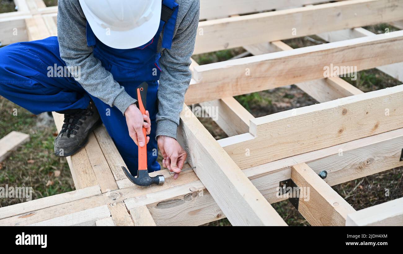 Man worker building wooden frame house on pile foundation. Carpenter ...