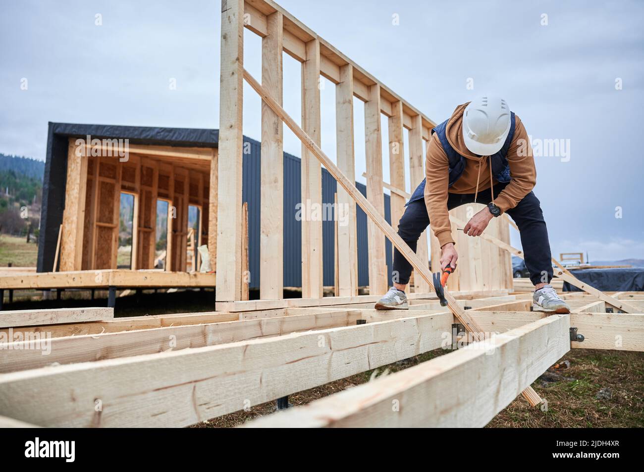 Man worker building wooden frame house on pile foundation. Carpenter ...