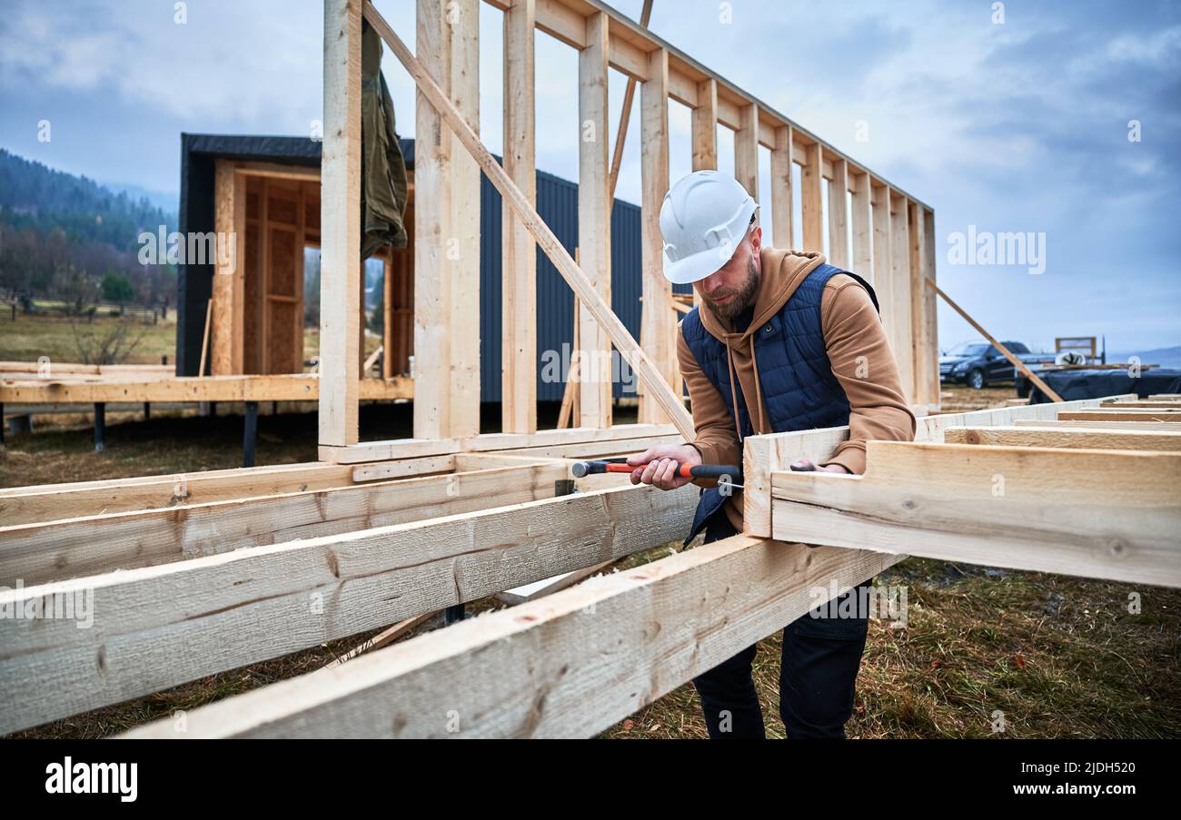 Man worker building wooden frame house on pile foundation. Carpenter ...