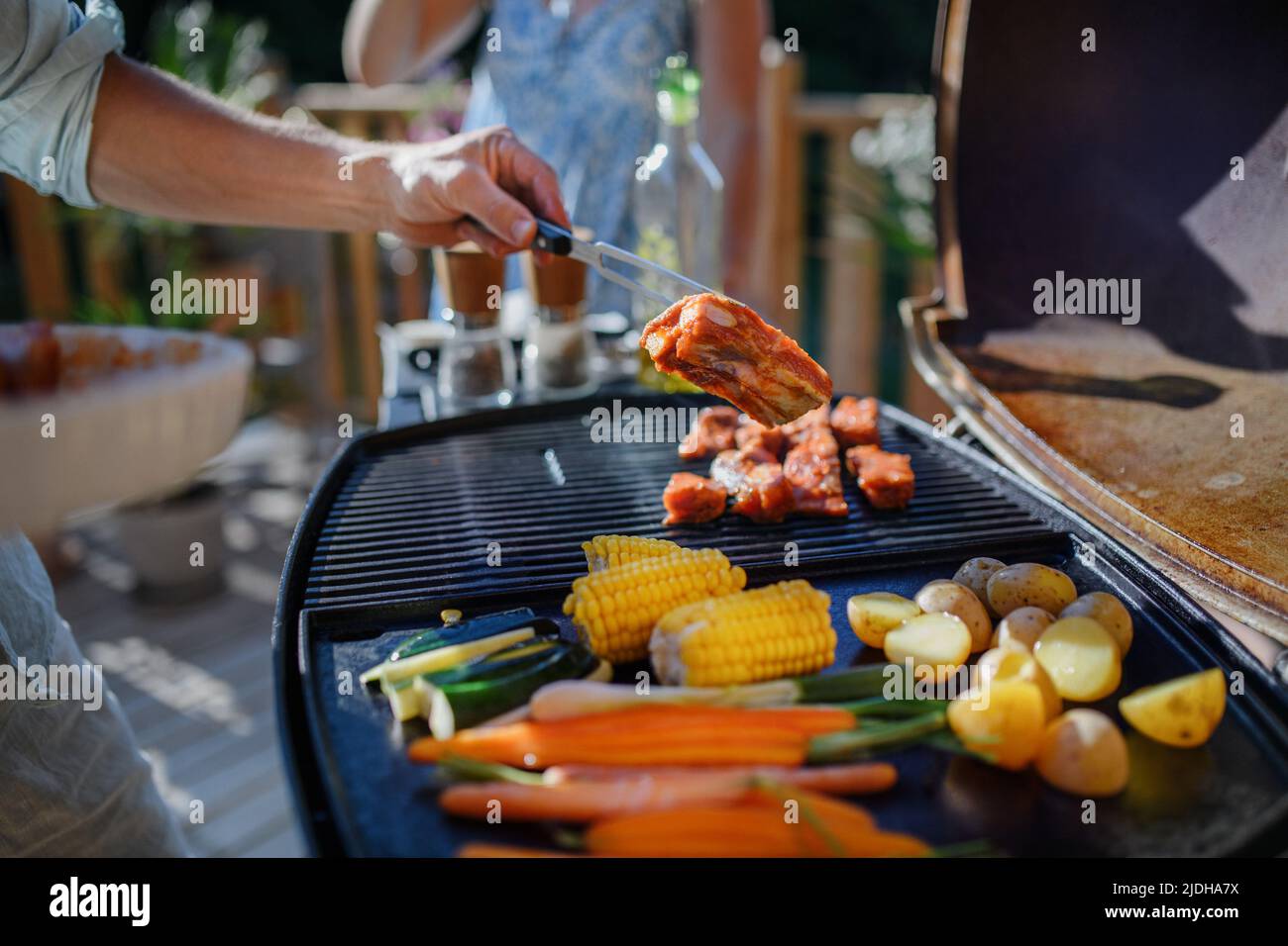 Unrecognizable man grilling ribs and vegetable on grill during family ...