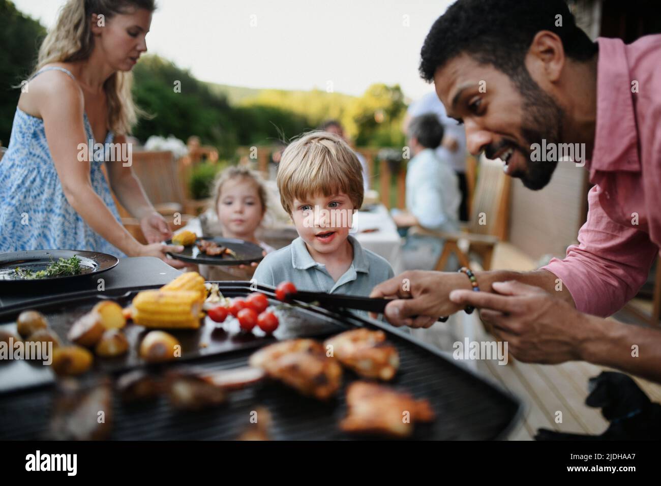 Father grilling meat and vegetable on grill during family summer garden ...