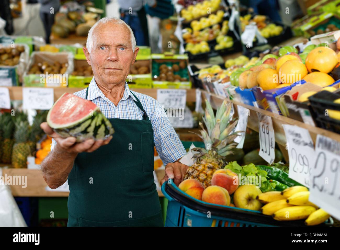 Positive senior male owner of greengrocery shop in apron offering fresh ...