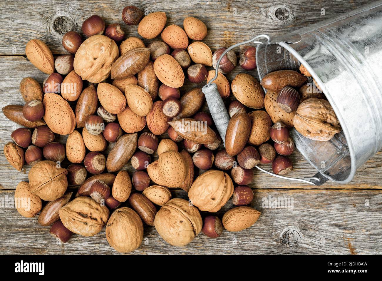 Tiny metal bucket and assorted nuts on a wooden background. Nuts are a ...