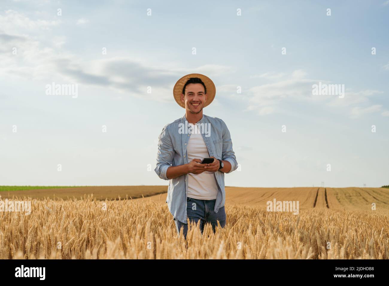 Happy farmer using mobile phone while standing in his growing wheat ...