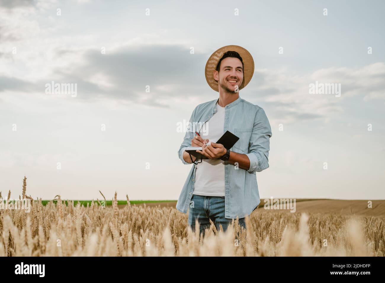 Happy farmer writing notes while standing in his growing wheat field ...
