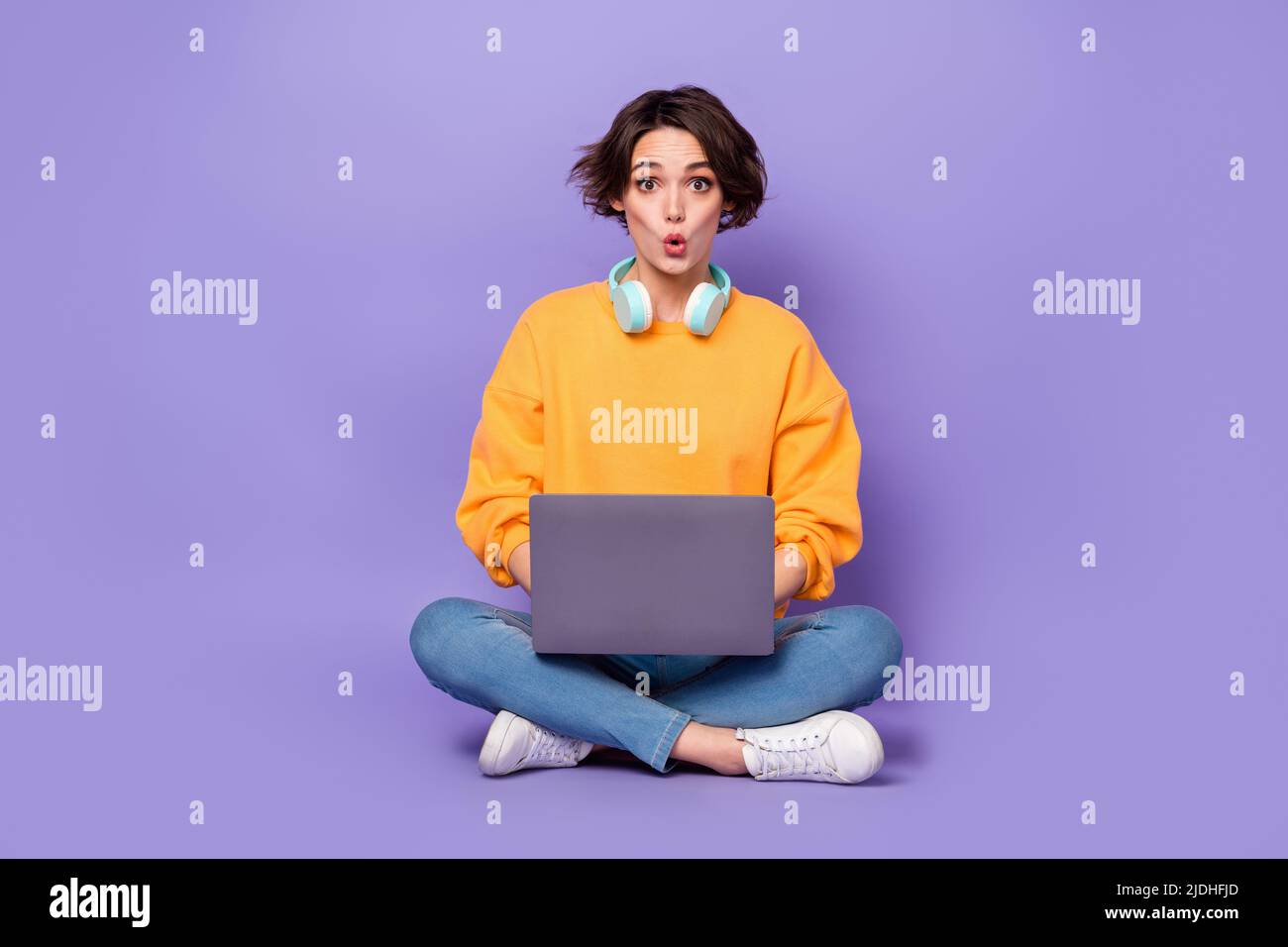 Portrait of attractive stunned girl sitting lotus pose using netbook ...