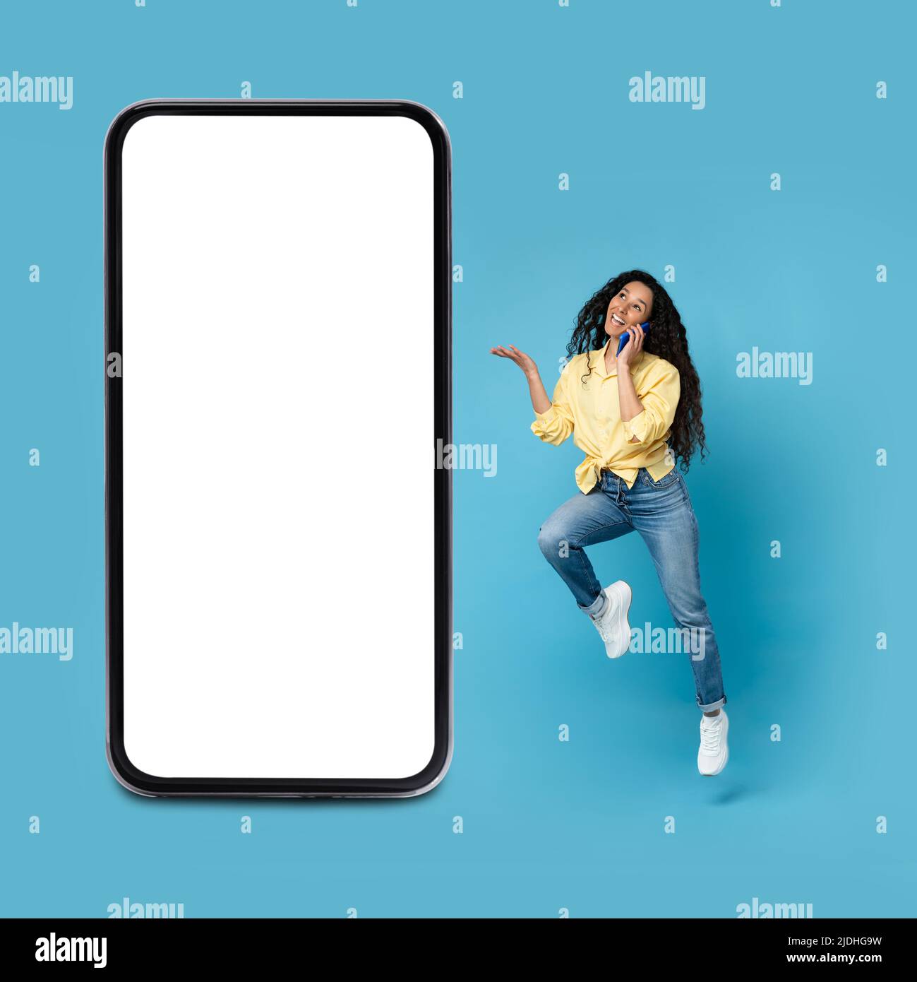 Young woman speaking on smartphone, jumping and running near huge ...