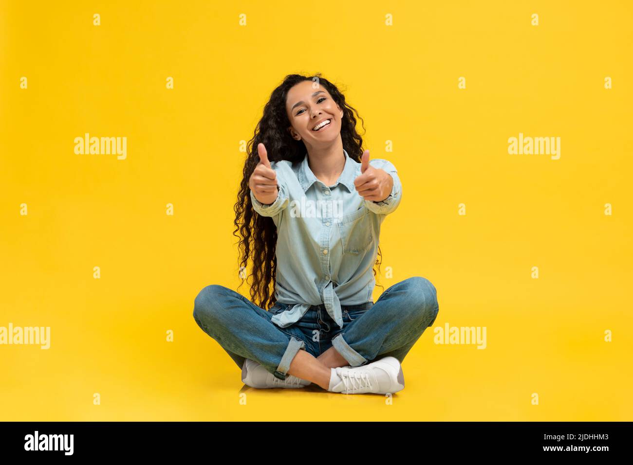 Smiling young woman gesturing thumbs up with both hands, recommending ...