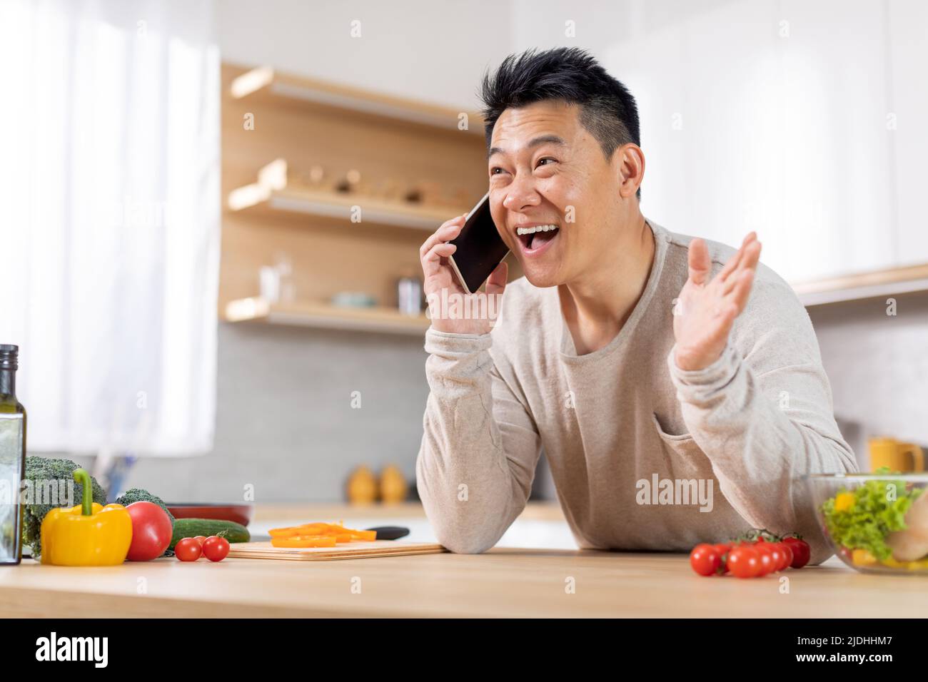 Happy asian man having phone conversation while cooking at home Stock ...