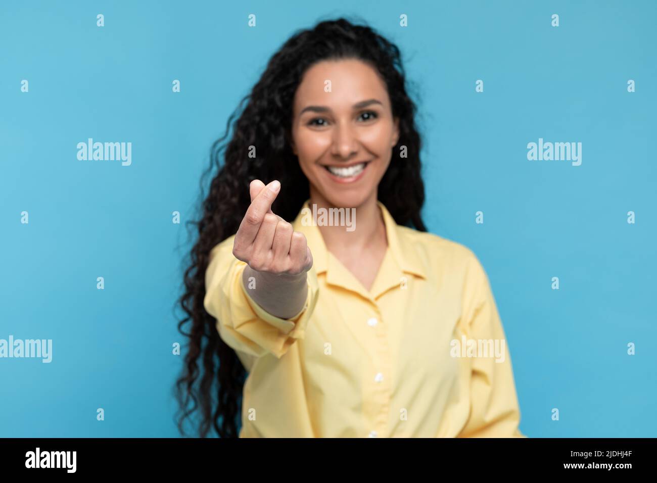 Beautiful young woman making Korean finger mini heart gesture on blue ...