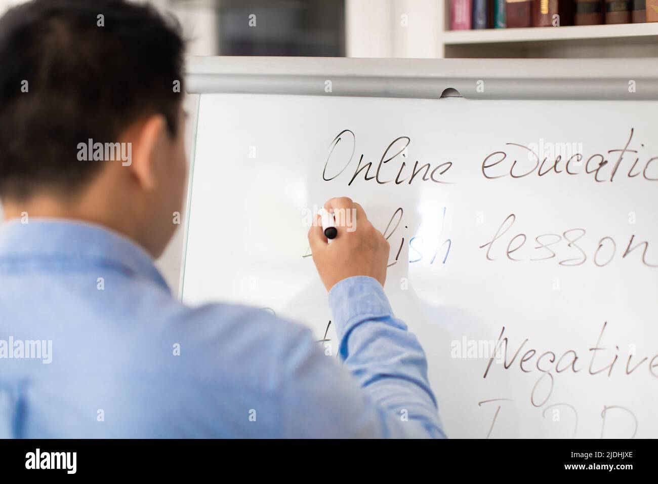 Asian Male Teacher Having Class Writing On Whiteboard In Classroom