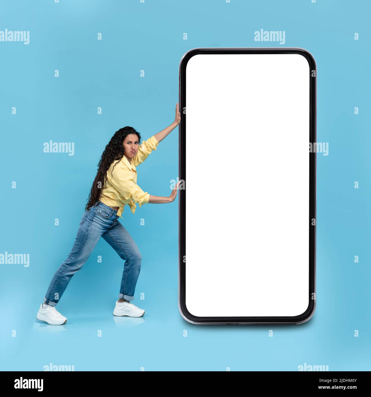 Emotional young woman pushing big heavy smartphone with empty screen on ...