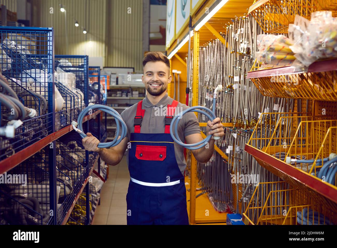Happy male shop assistant at DIY store smiling and showing hoses for ...