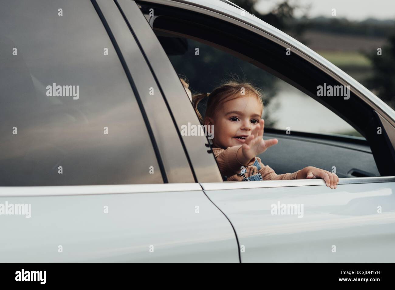 Little Girl Looking Out of a Car Window and Waves Her Hand Showing ...