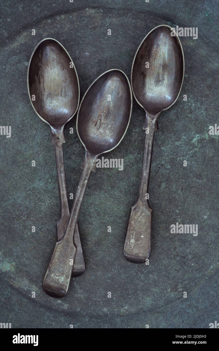 Three antique tarnished silver teaspoons lying on tarnished metal plate ...