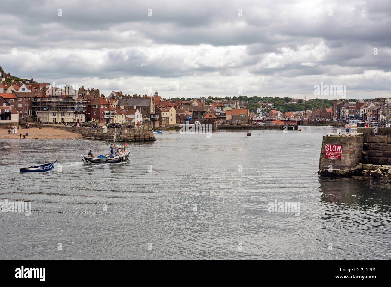 Fishing boat towing rowing boat entering urban part of RIver Esk ...