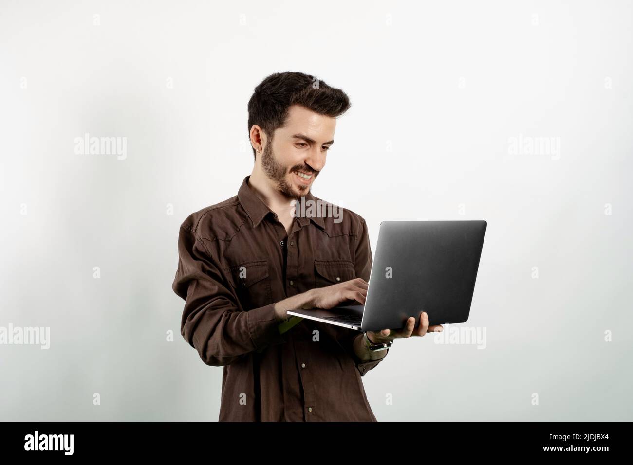 Cheerful young man wearing brown shirt posing isolated over white ...