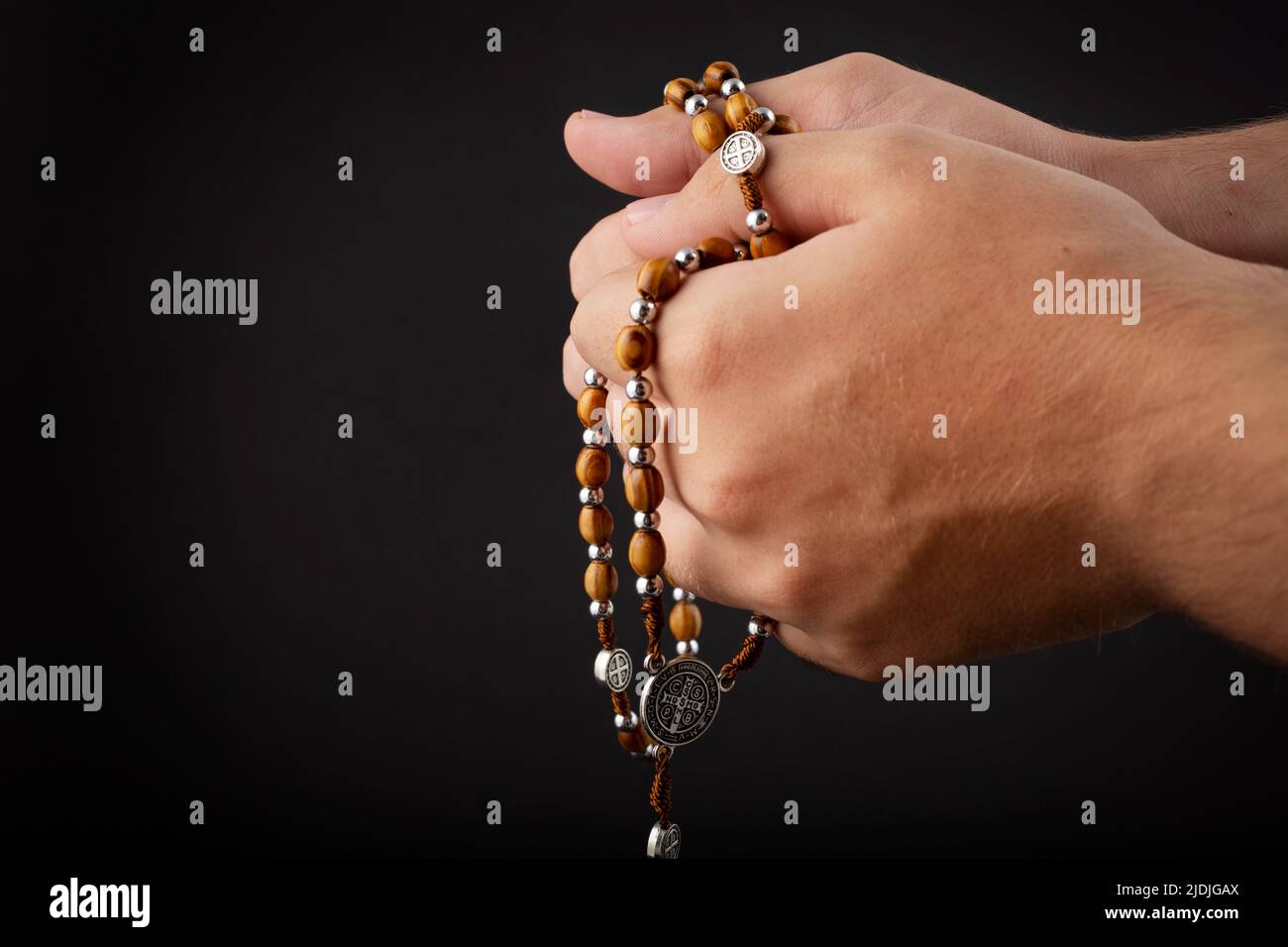 Folded hands of a young man holding a rosary during a pray isolated on ...