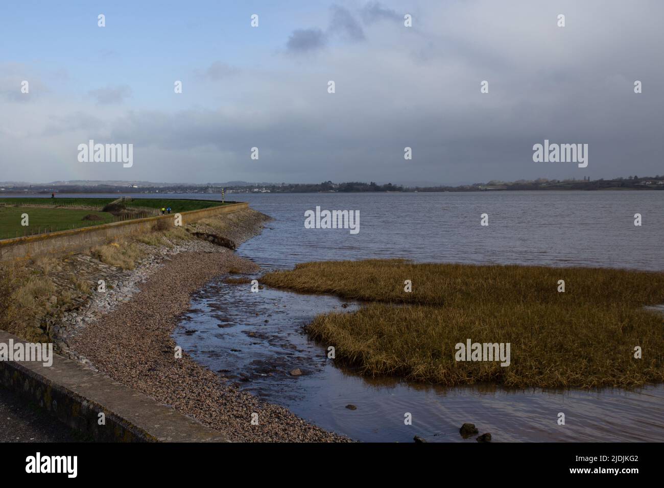 sea defences and wall with footpath with still water and blue sky with ...